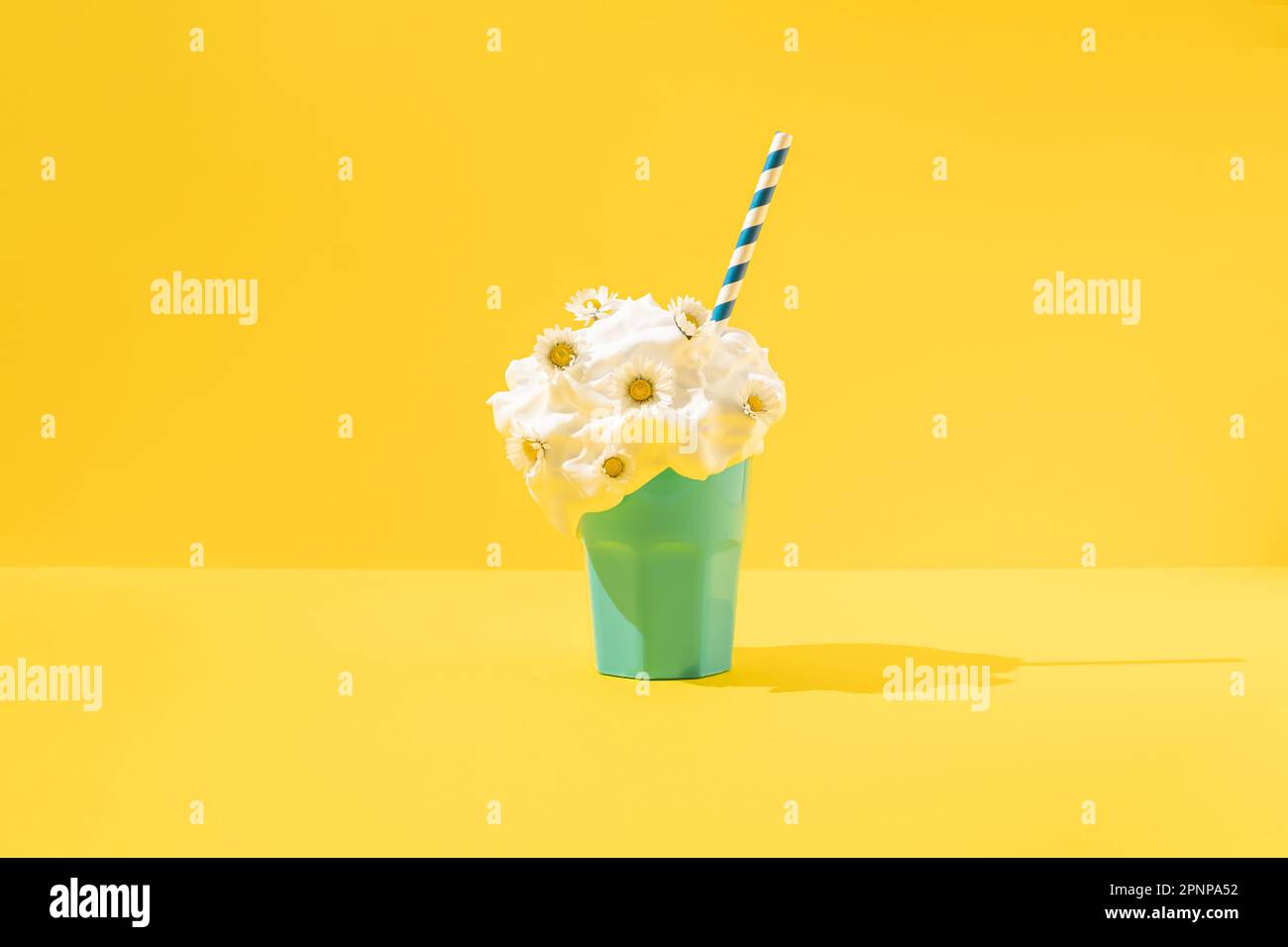 Creamy milkshake with daisy flowers and paper straw on yellow ...