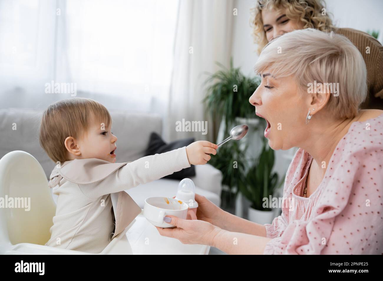 side view of little child with spoon feeding grandmother with bowl in ...