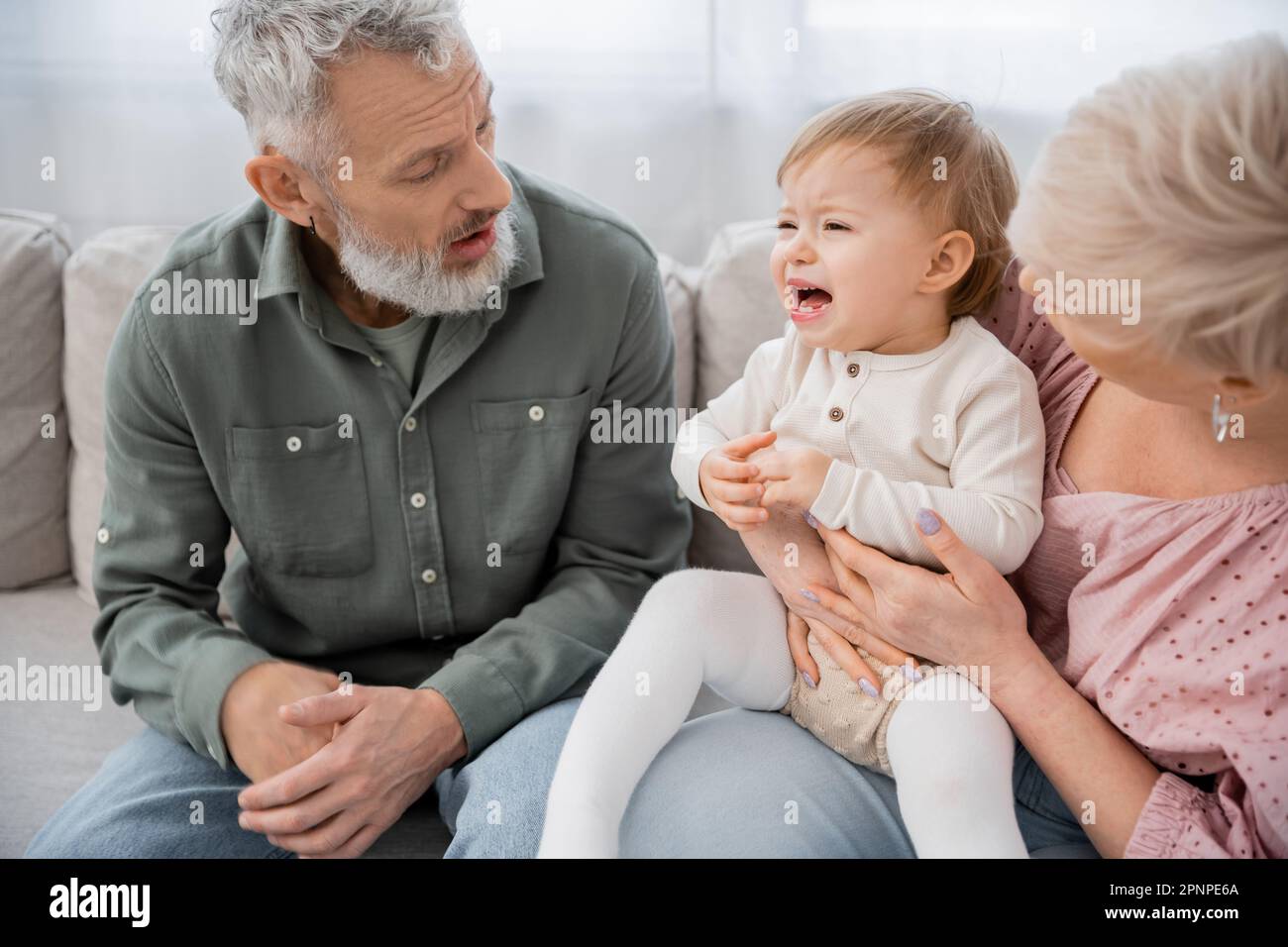confused middle aged couple calming crying granddaughter on couch in ...