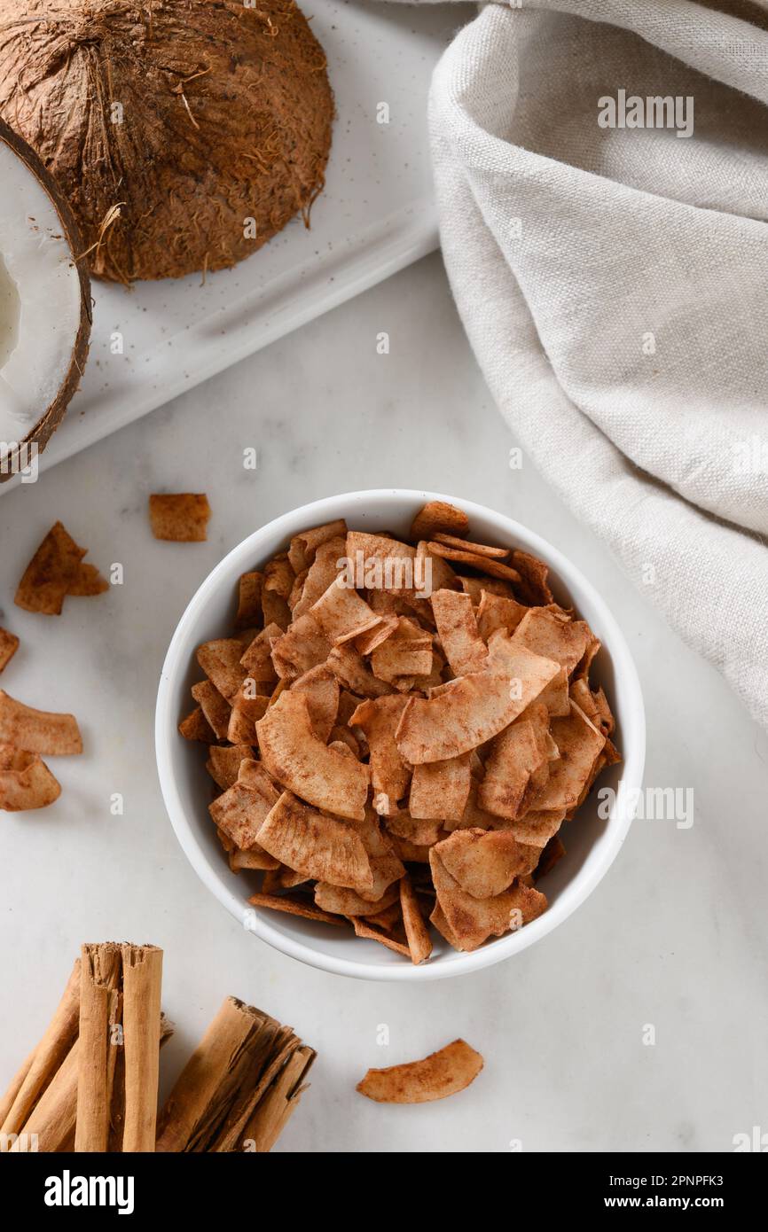 Coconut chips with cinnamon in glass jar on white background, home drying. Vegan and sugar free ...