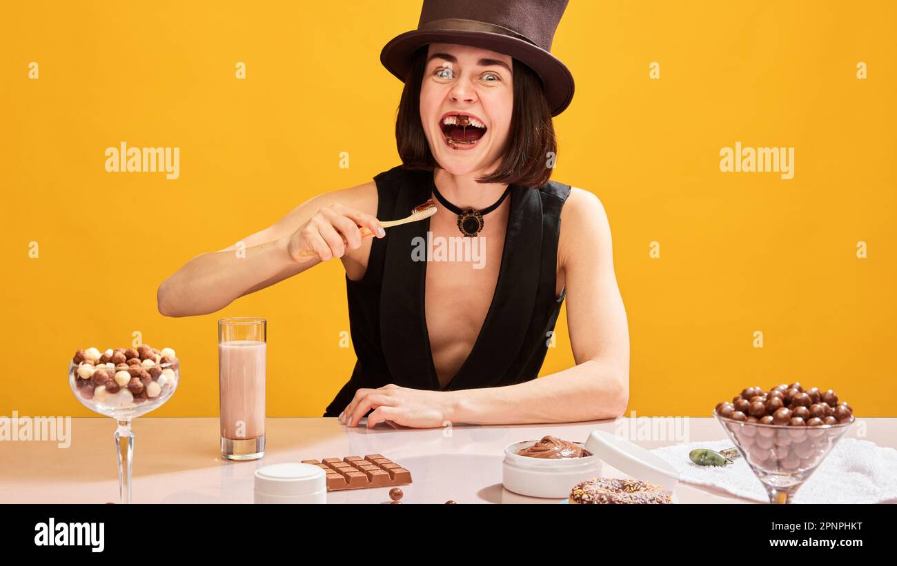 Crazy face. Smiling woman in cylinder brushing teeth with chocolate ...