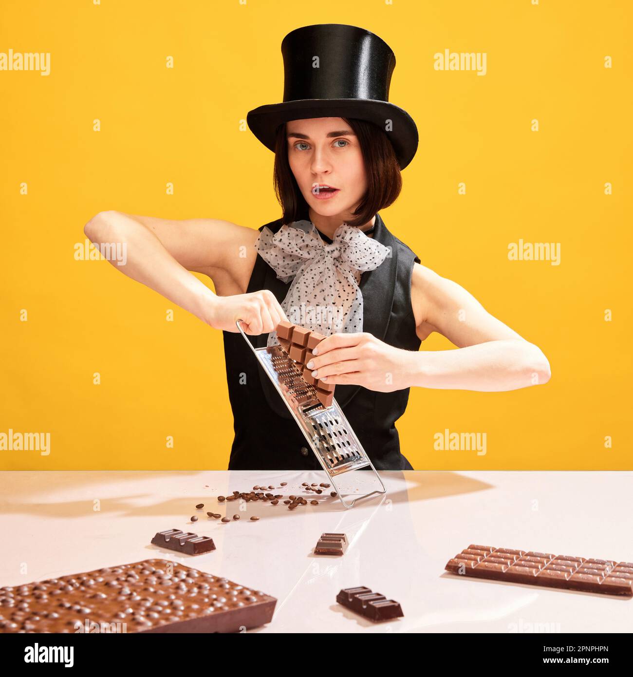 Artistic, beautiful woman in cylinder hat grating chocolate on grater ...