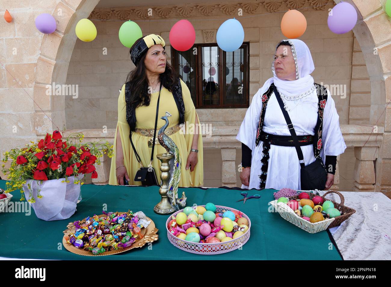Two Yazidi women stand at a table with candy and Turkish delight treats ...