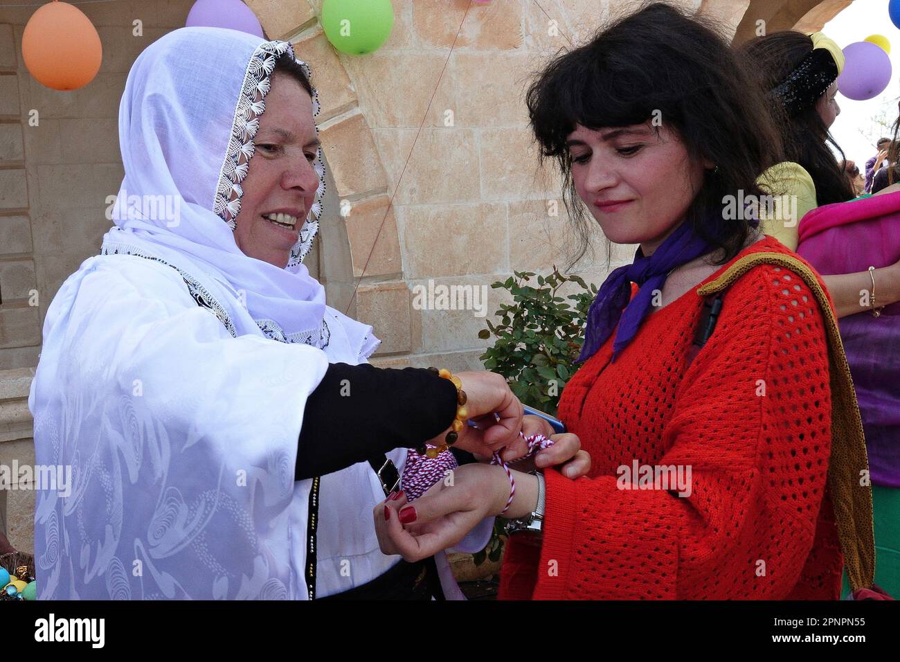 A Yazidi woman ties a colorful rope to a young girl's wrist during ...