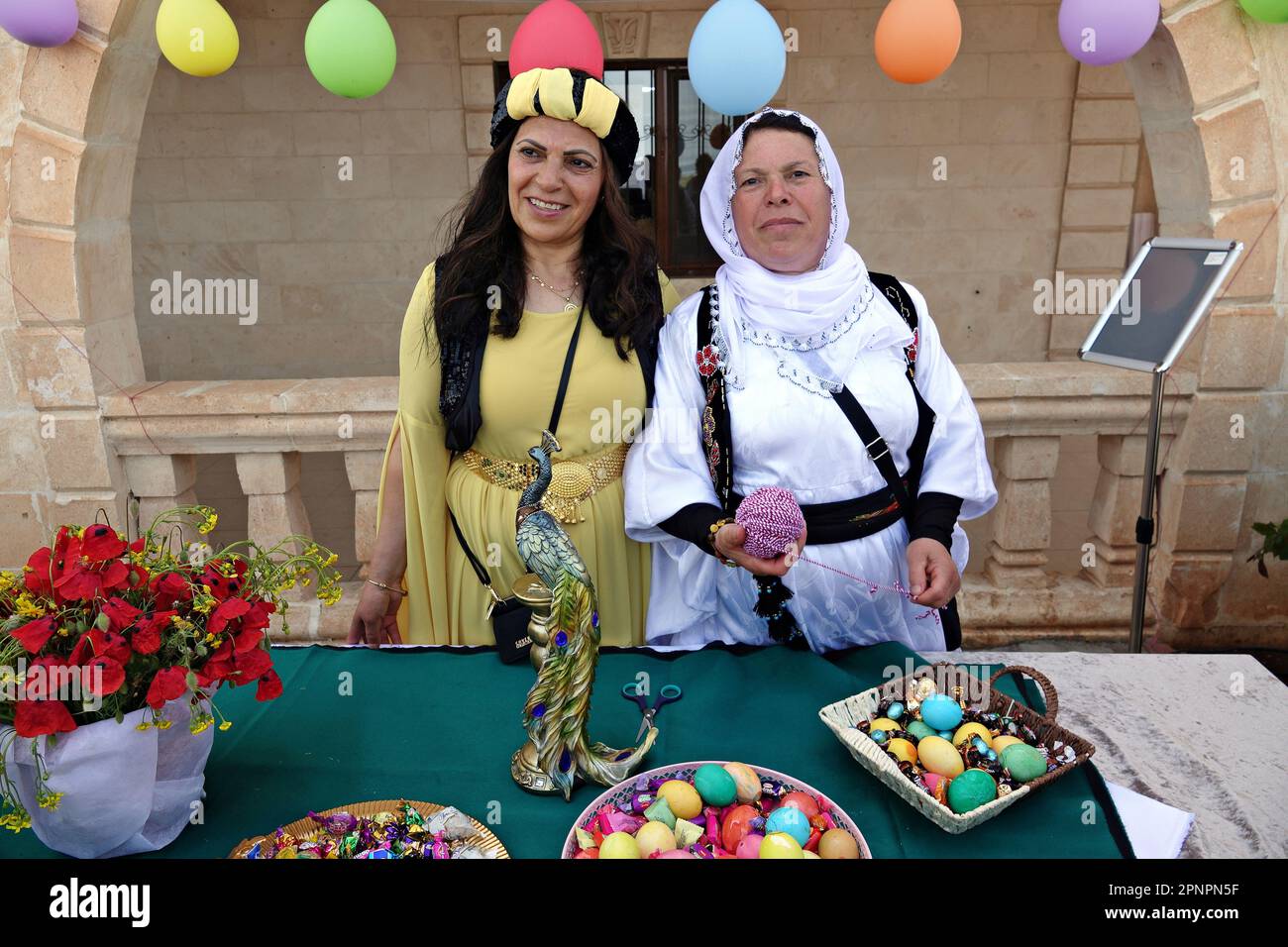 Two Yazidi women stand at a table with candy and Turkish delight treats ...