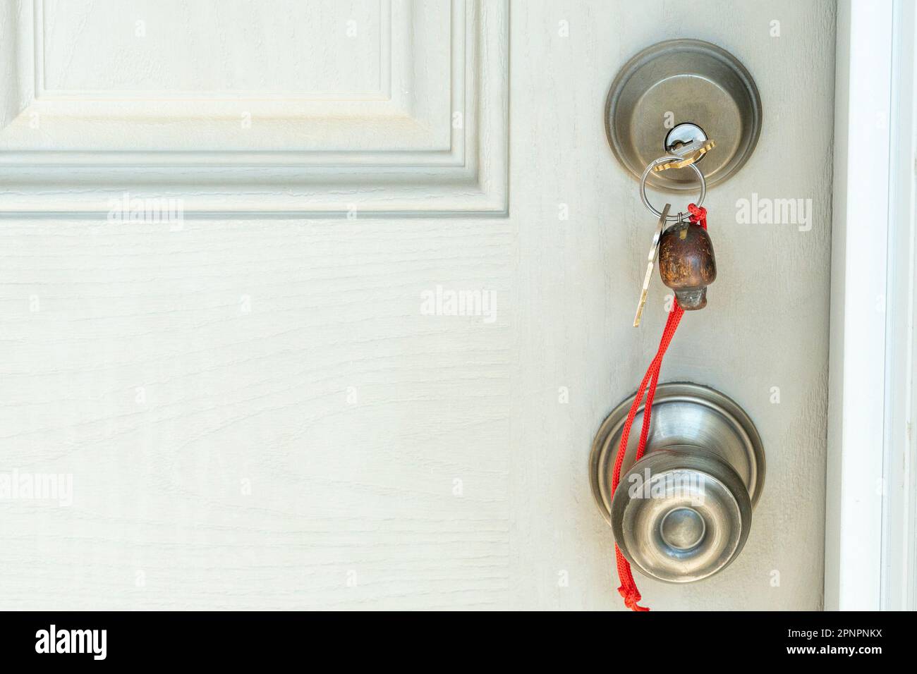 A key with a keychain on a red rope is inserted into the door lock ...