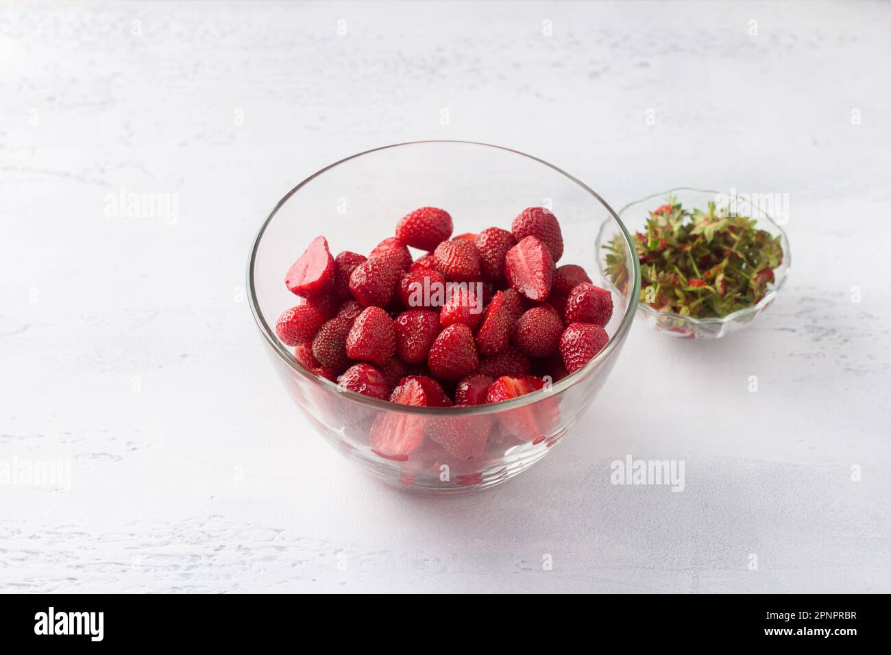 Glass bowl with peeled and chopped strawberries and a bowl with sepals ...