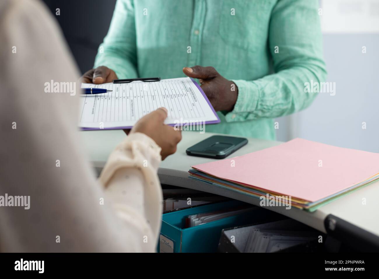 Midsection of biracial medical receptionist handing documents to ...