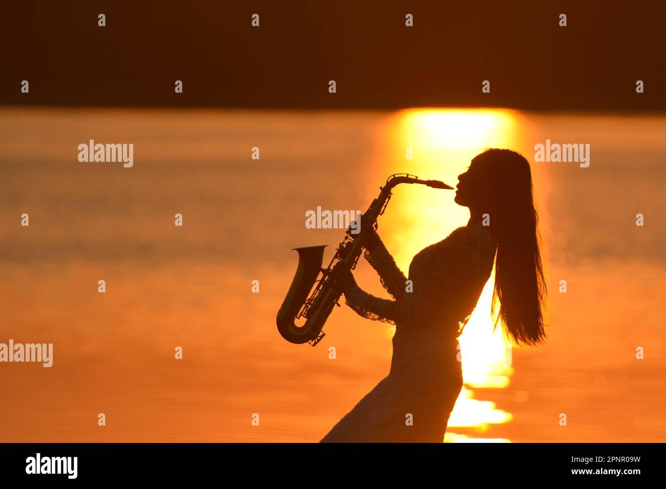 Silhouette of a female saxophonist playing the saxophone by a lake at ...