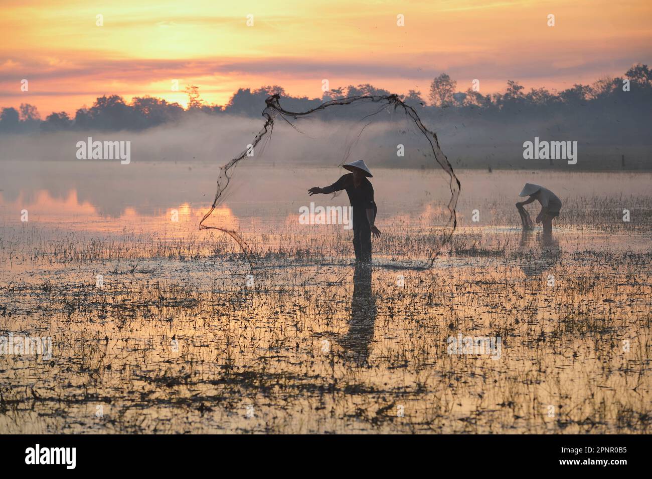 Silhouette of two fishermen standing in a river throwing fishing nets ...