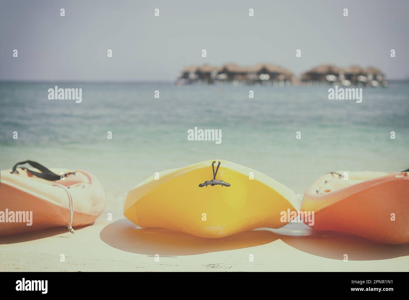 Close-up of three canoes in a row on the beach with huts in the ...