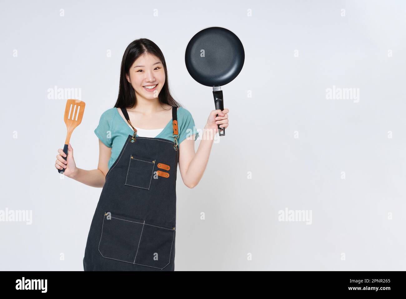 Young woman wearing kitchen apron cooking and holding pan and spatula ...