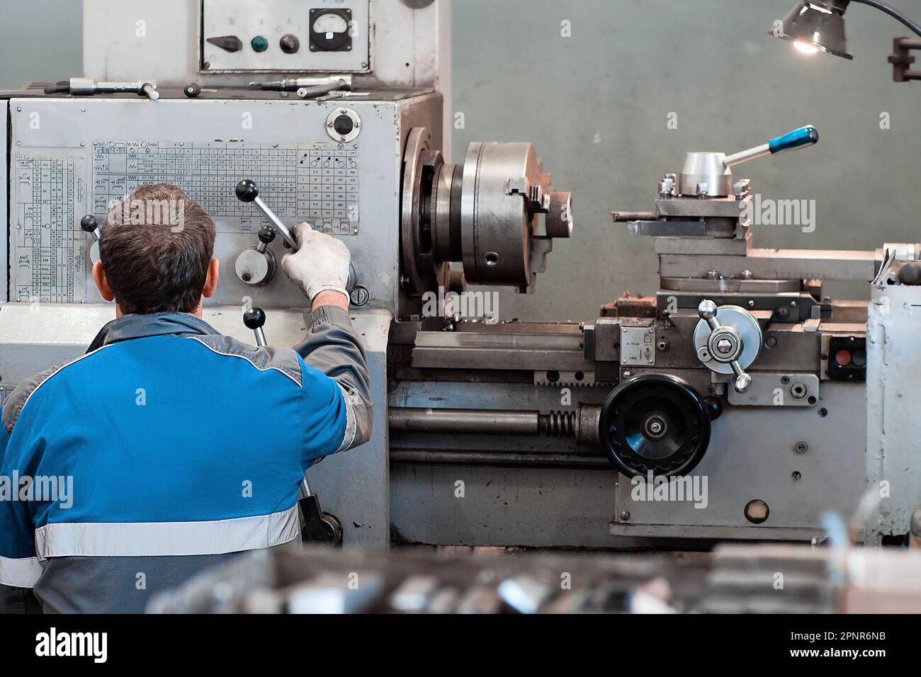 Turner at lathe in workplace. View of worker from back. Metal ...