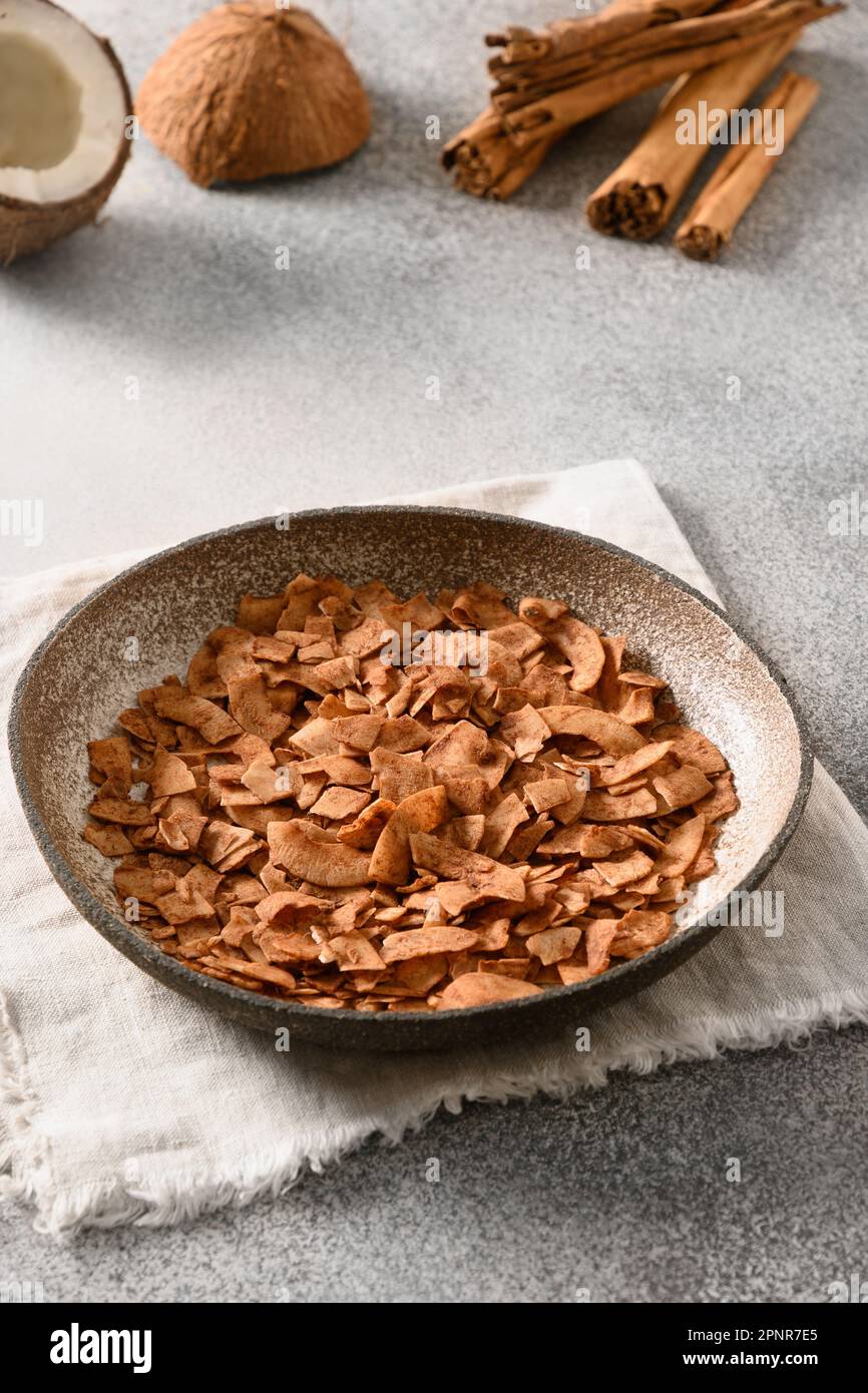 Coconut chips with cinnamon in glass jar on gray background, home drying. Vegan and sugar free ...