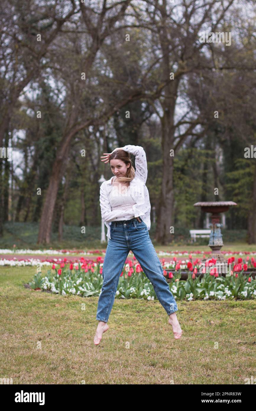 Young woman dancing in the park, in the middle of an elegant jump move ...
