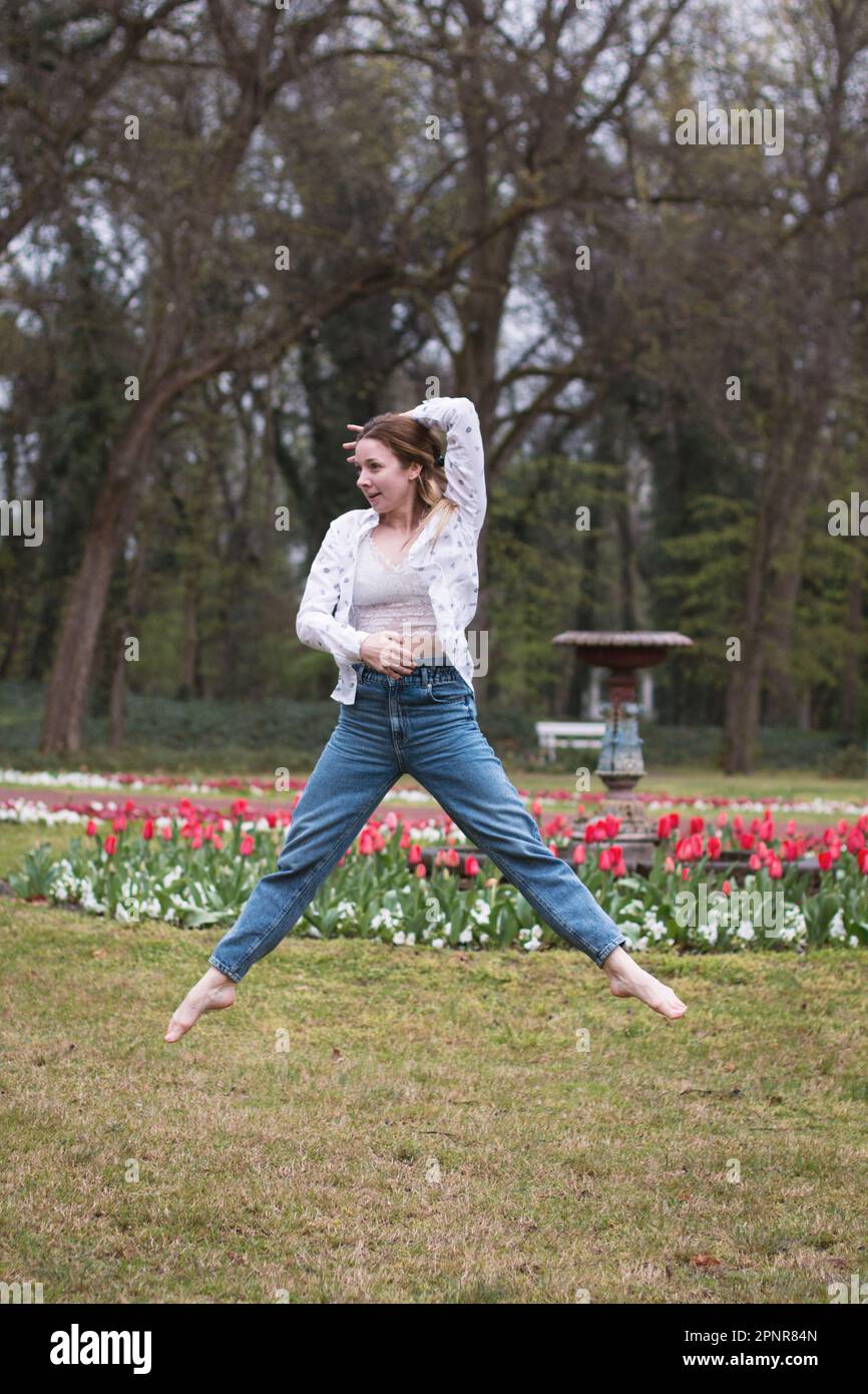 Young woman dancing in the park, in the middle of an elegant jump move ...