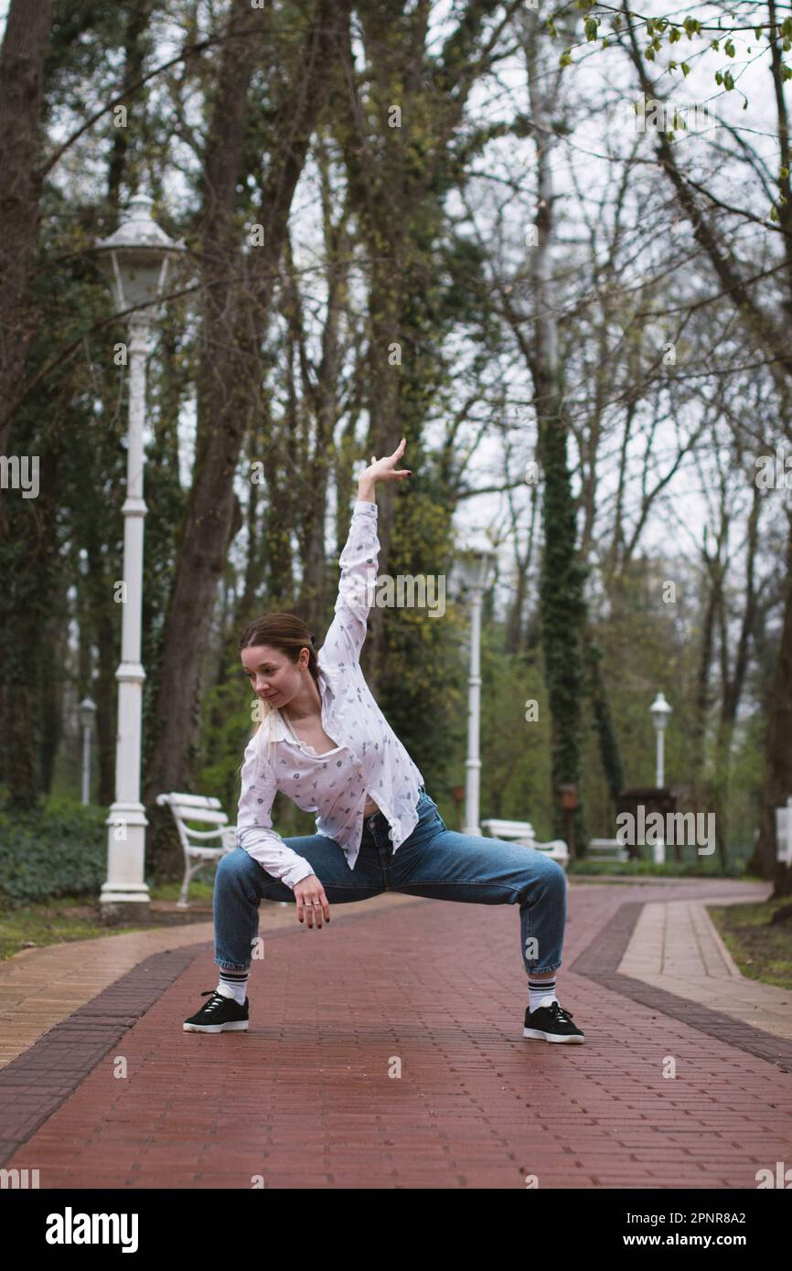 Young woman freestyle dancing in the park in the city, in rainy weather ...
