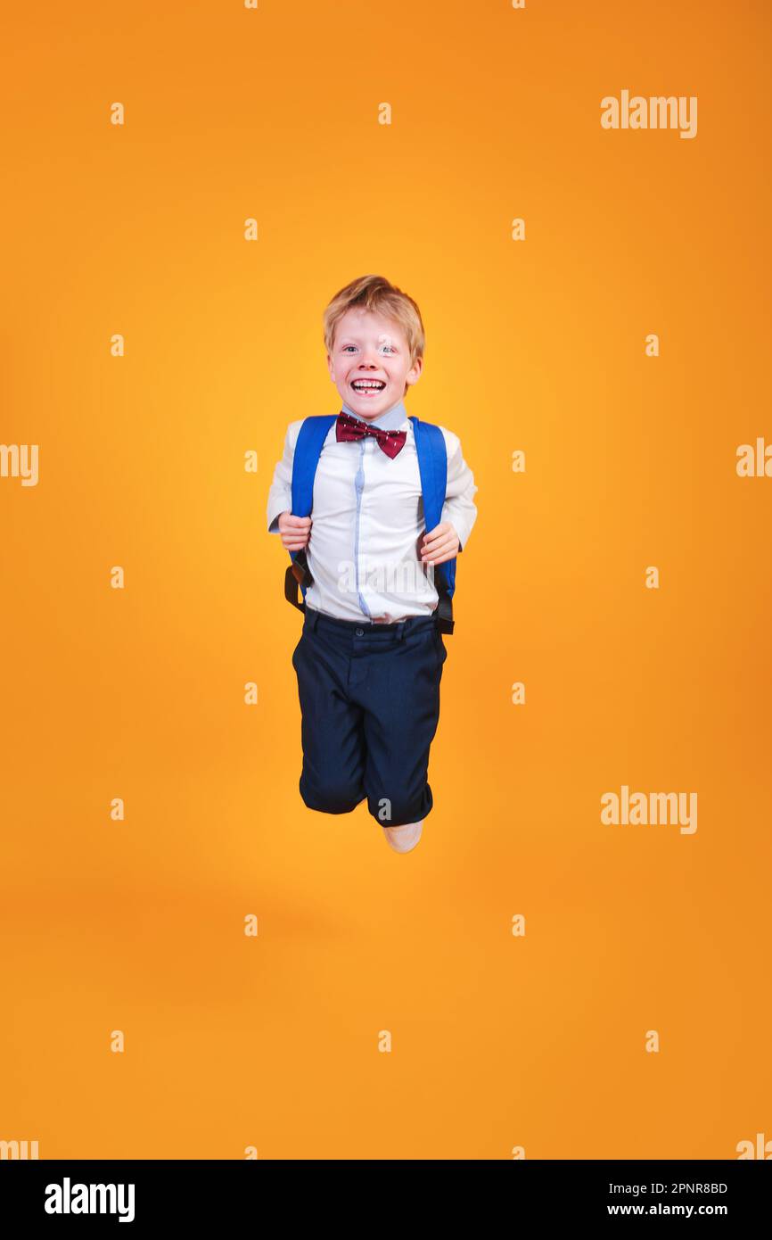 Funny school boy with a backpack jumping on yellow studio background ...