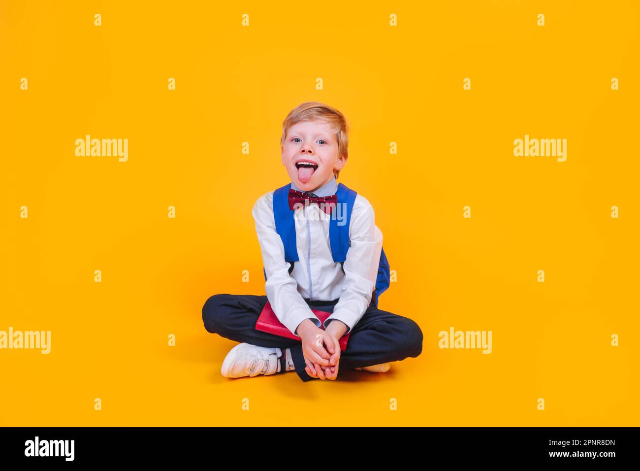 Funny school boy showing tongue at camera and sitting on yellow ...