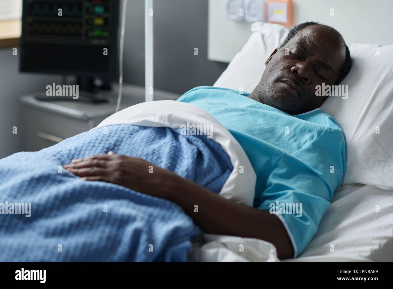 African American unconscious patient lying on bed in hospital ward with monitor checking his ...