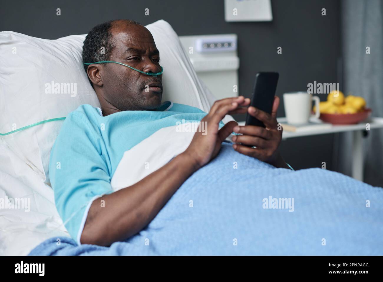 African American elderly patient using smartphone while lying on bed in ...