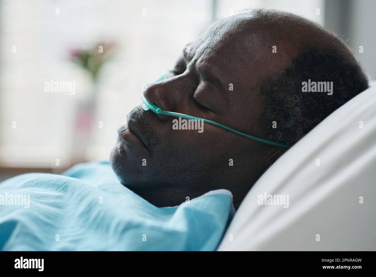 African American man breathing with oxygen tube while lying on bed in ...