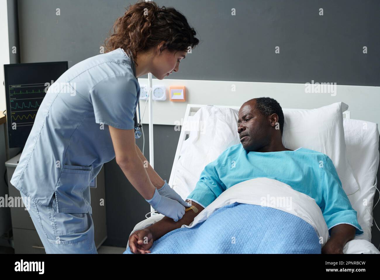 Young nurse making dropper for sick patient, she inserting catheter in ...