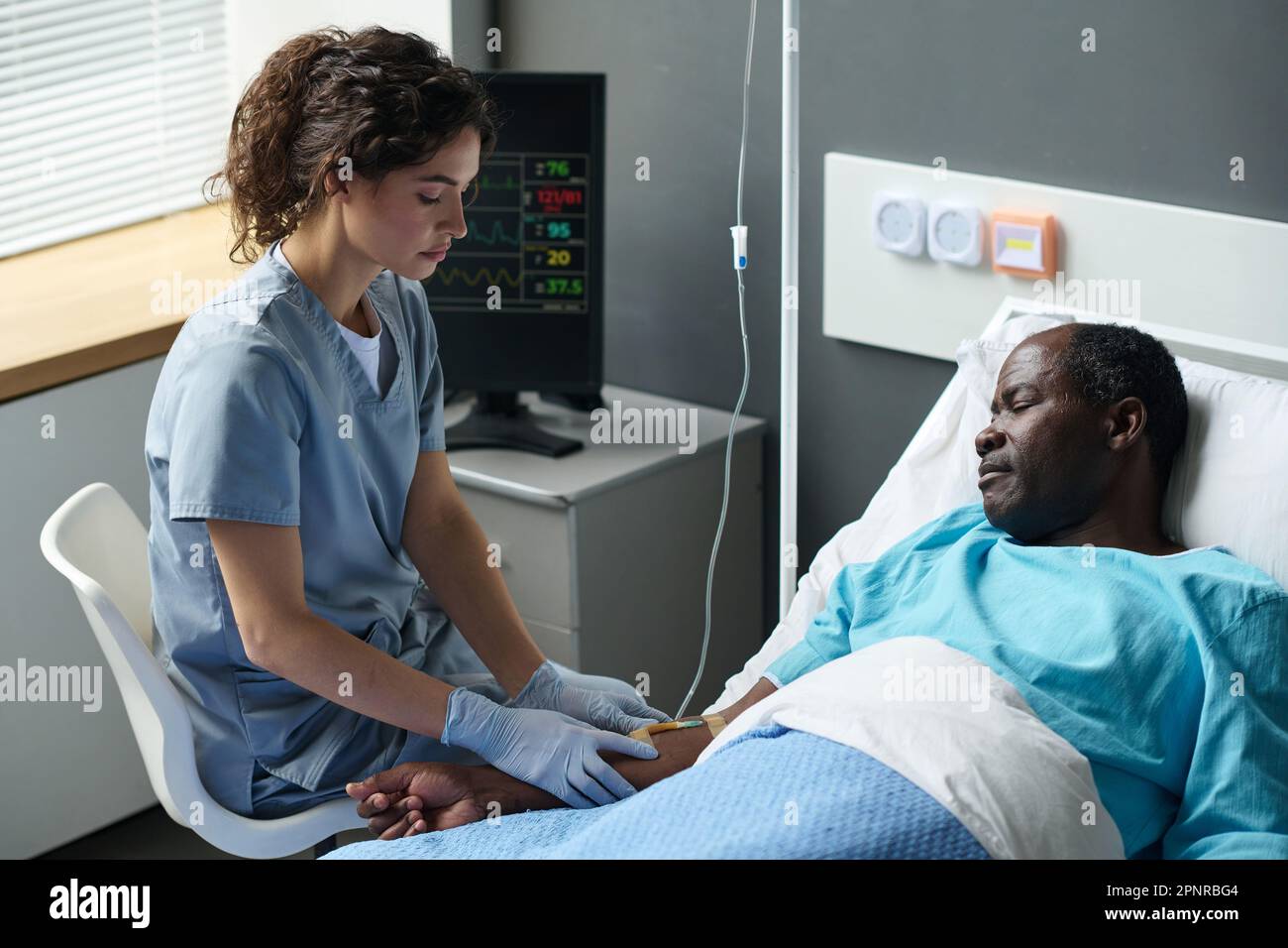 Young nurse in uniform making dropper for sick elderly patient while he ...