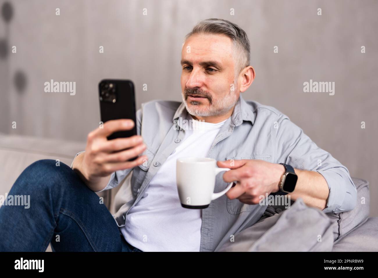 Man drinking coffee and using mobile phone at home, adult caucasian ...