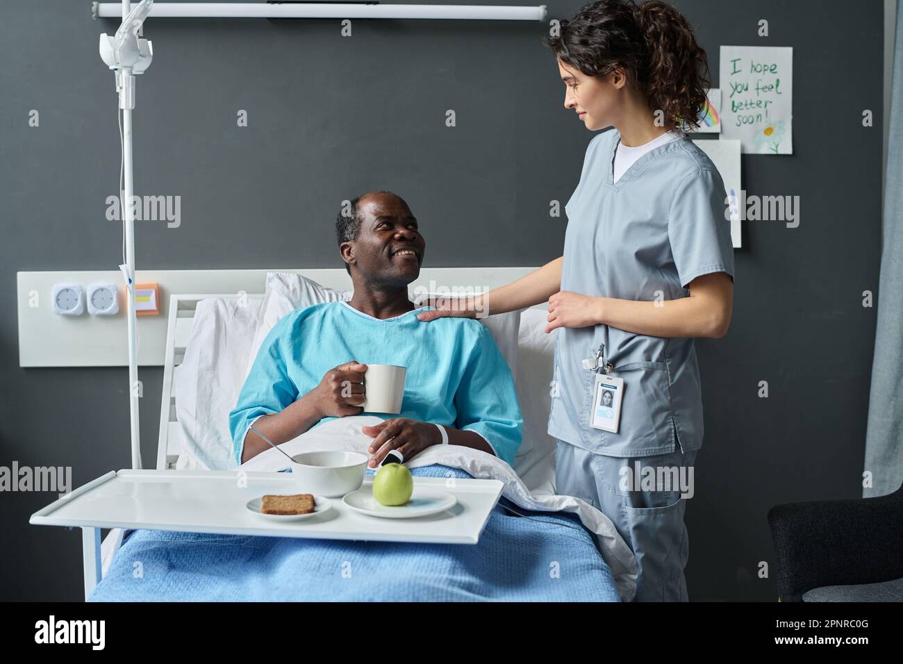Young nurse in uniform serving lunch to senior patient while he sitting ...