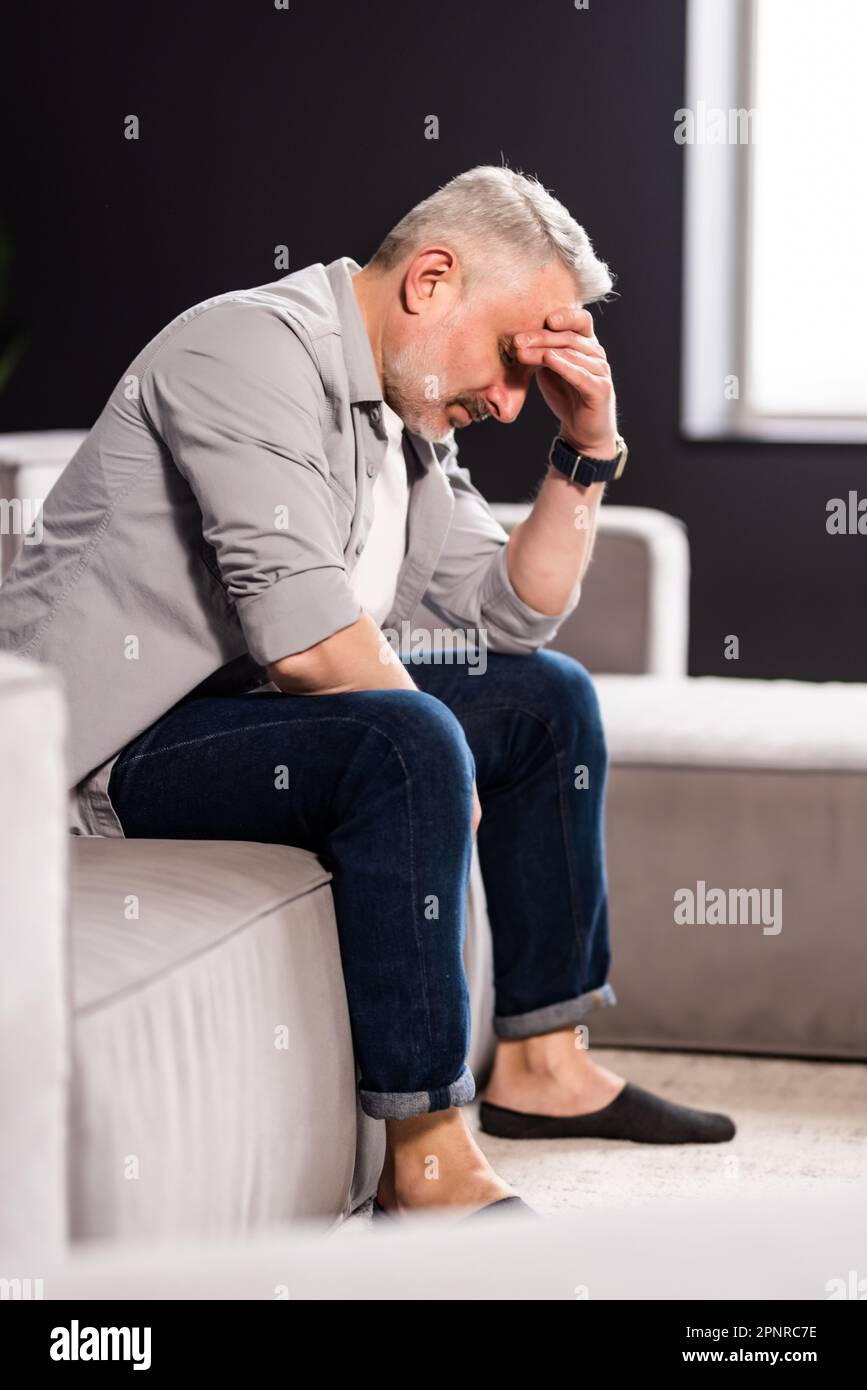 Frustrated middle aged man sitting on couch at home. Close up face of ...