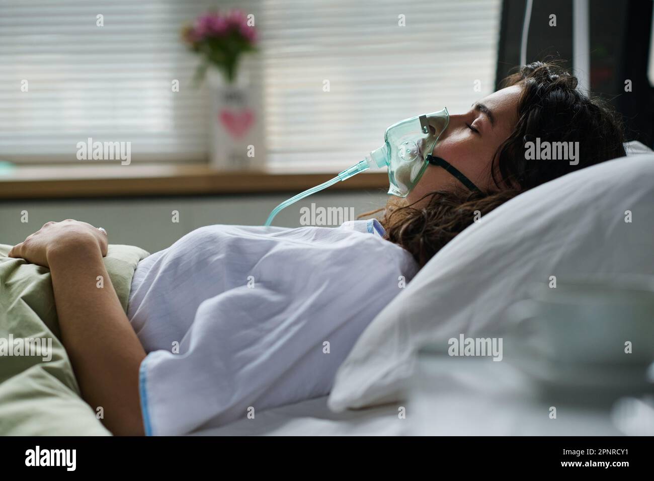 Young Woman Breathing With Oxygen Mask Lying On Bed During Treatment In