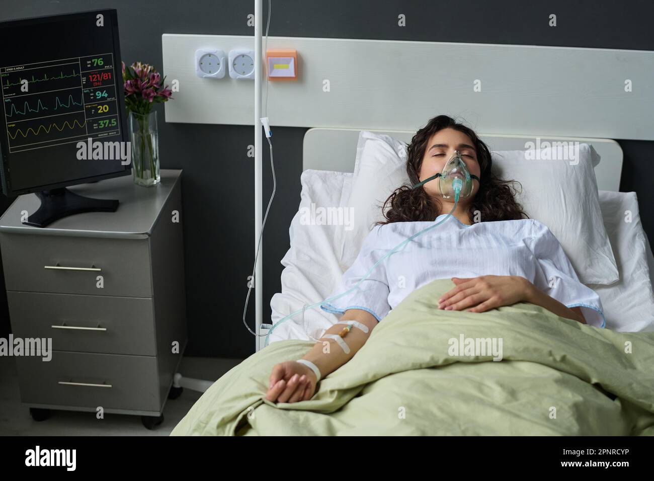 Unconscious young woman lying on bed with oxygen mask during treatment ...