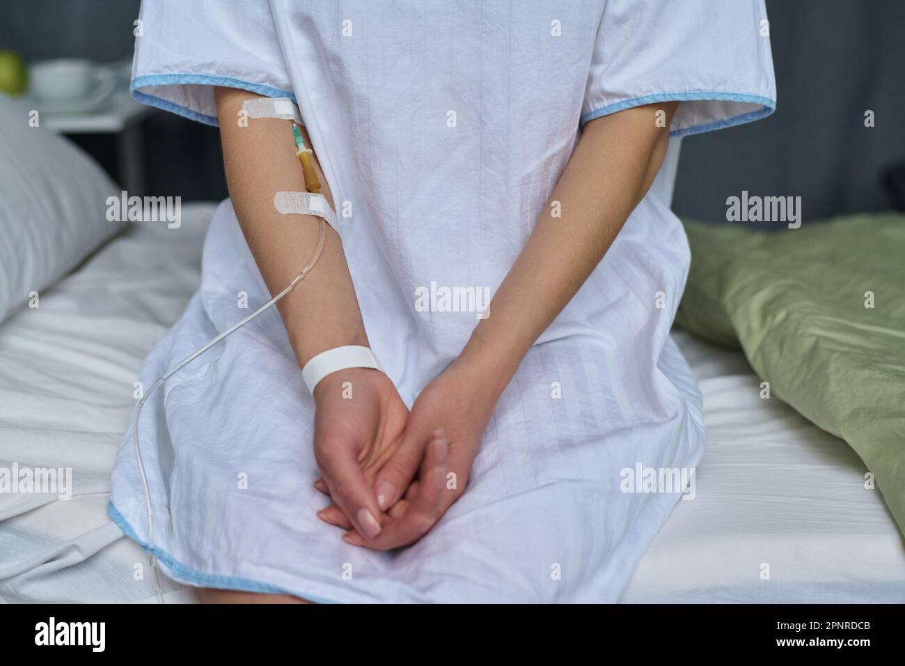 Close-up of young patient with catheter in her arm sitting on bed in ...