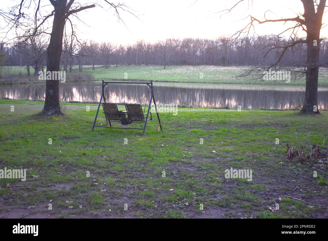 A camouflage colored swing sits in the yard near a pond, a relaxing ...