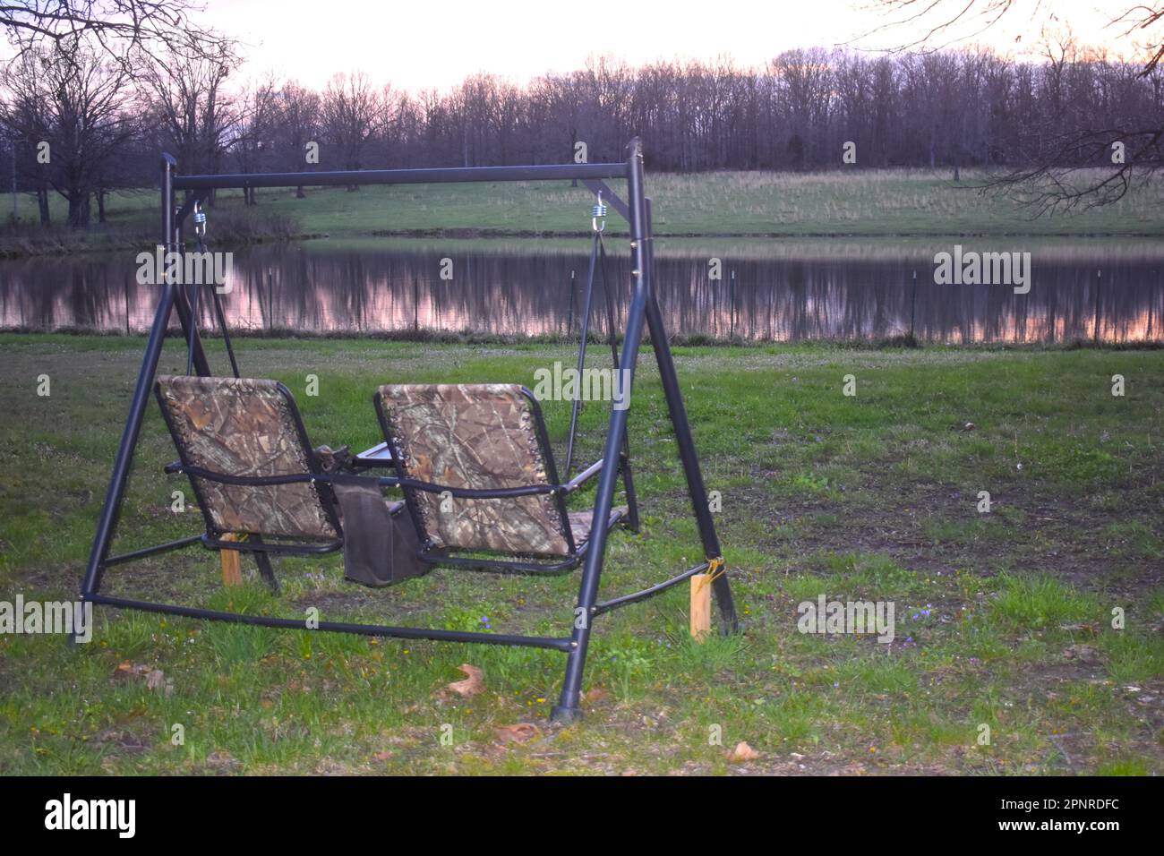 A camouflage colored swing sits in the yard near a pond, a relaxing ...