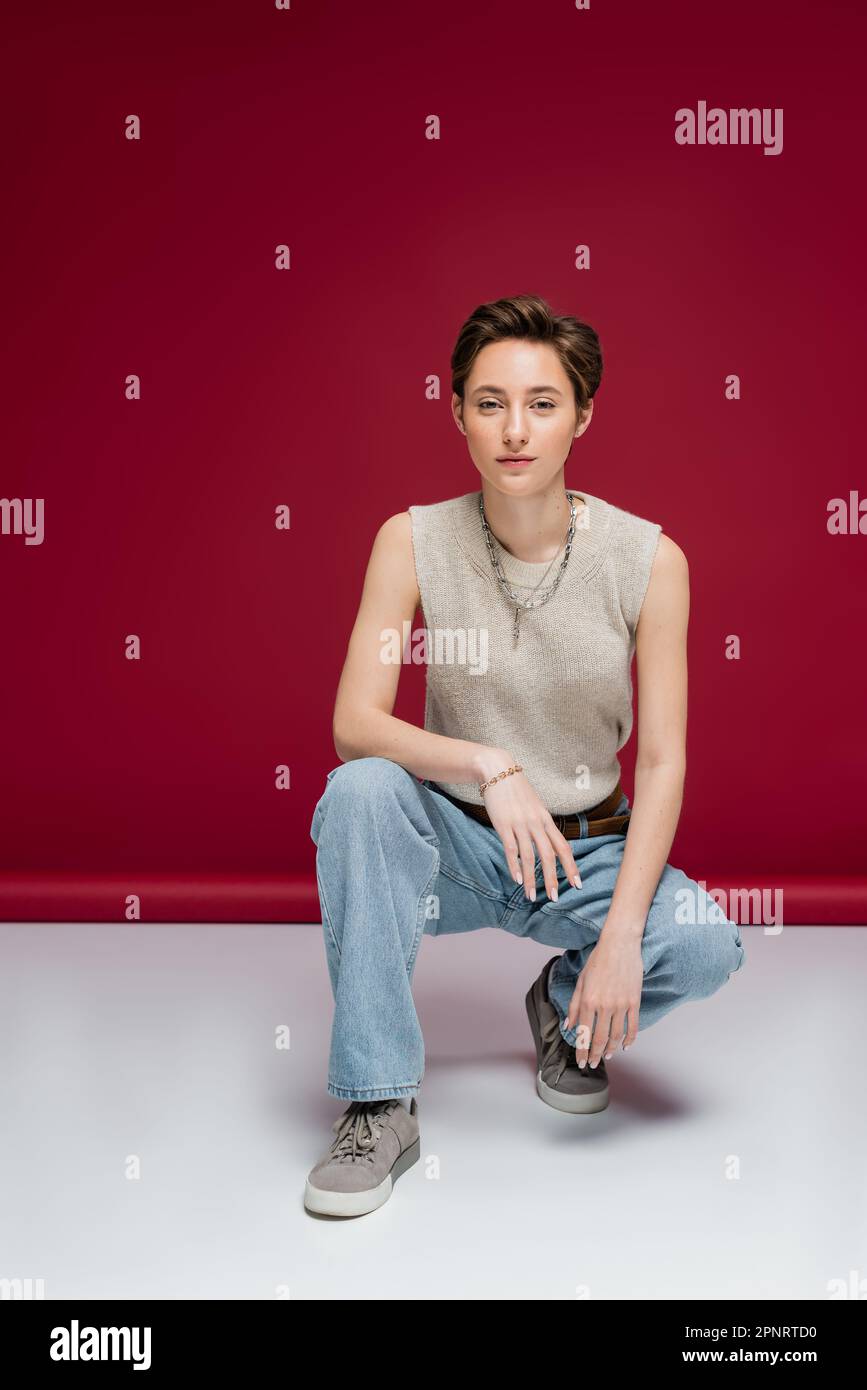 full length of pretty young woman with short hair sitting on haunches ...