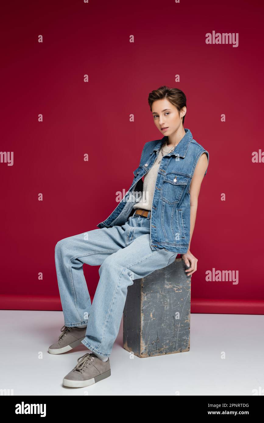 full length of pretty young model with short hair sitting in denim ...