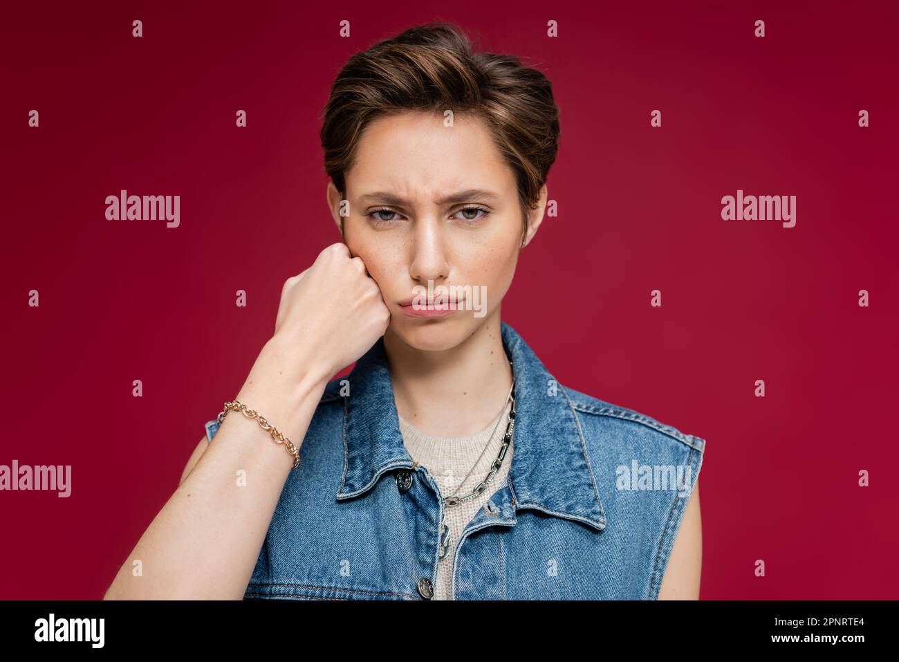 sad young woman with short hair looking at camera on burgundy ...