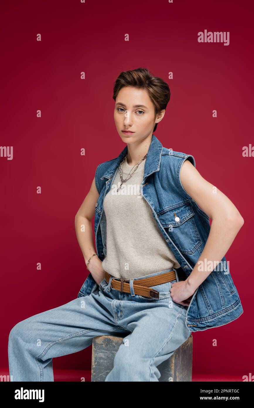 stylish model in denim outfit with vest posing with hands on hips on ...