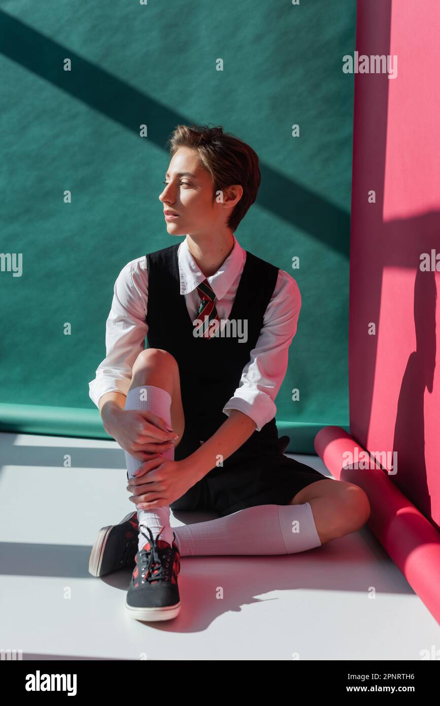 full length of stylish young student with short hair sitting in school ...