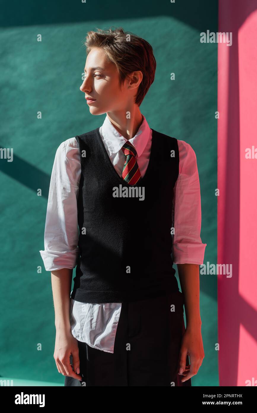 stylish student with short hair standing in school uniform on pink and ...