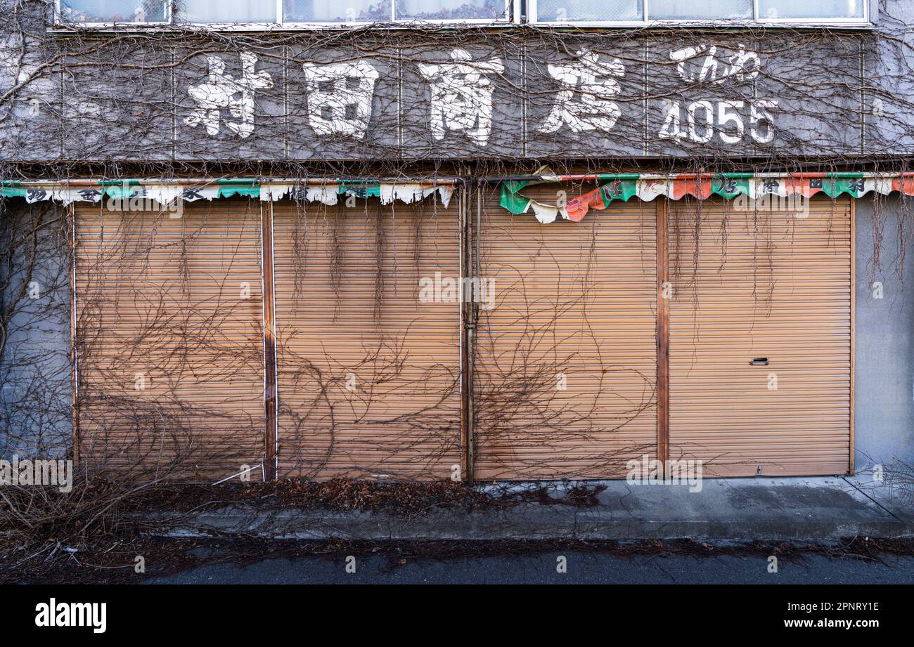 A defunct business with vines growing on the building in Kuji, Iwate ...