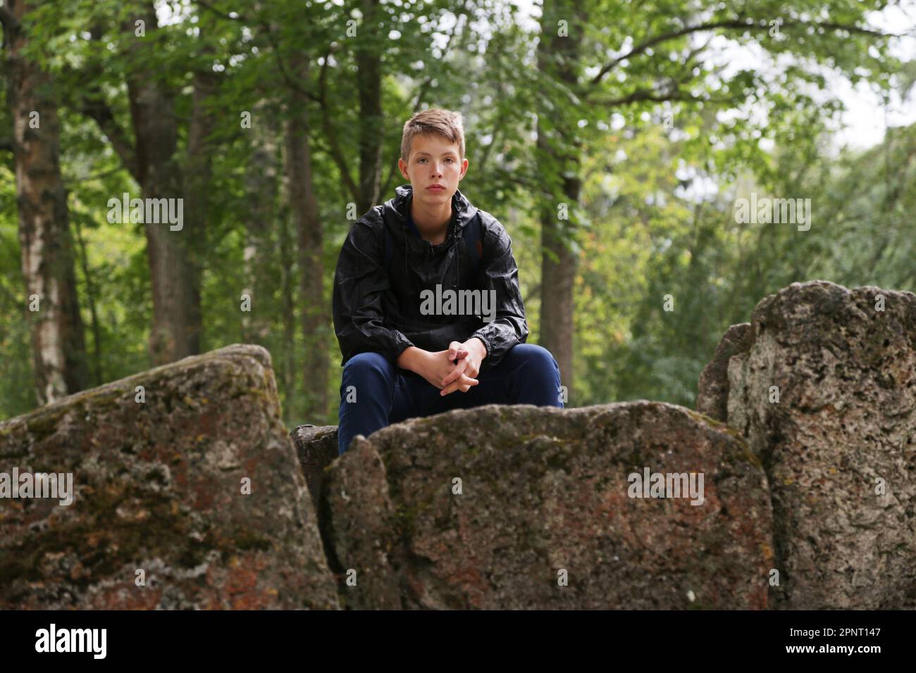 Portrait of a teenager boy sitting on large stones Stock Photo - Alamy
