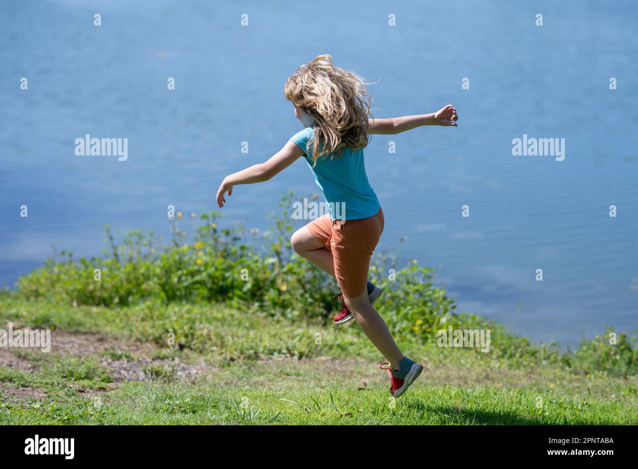 Kid boy running on green grass near lake in summer park. Kid boy ...