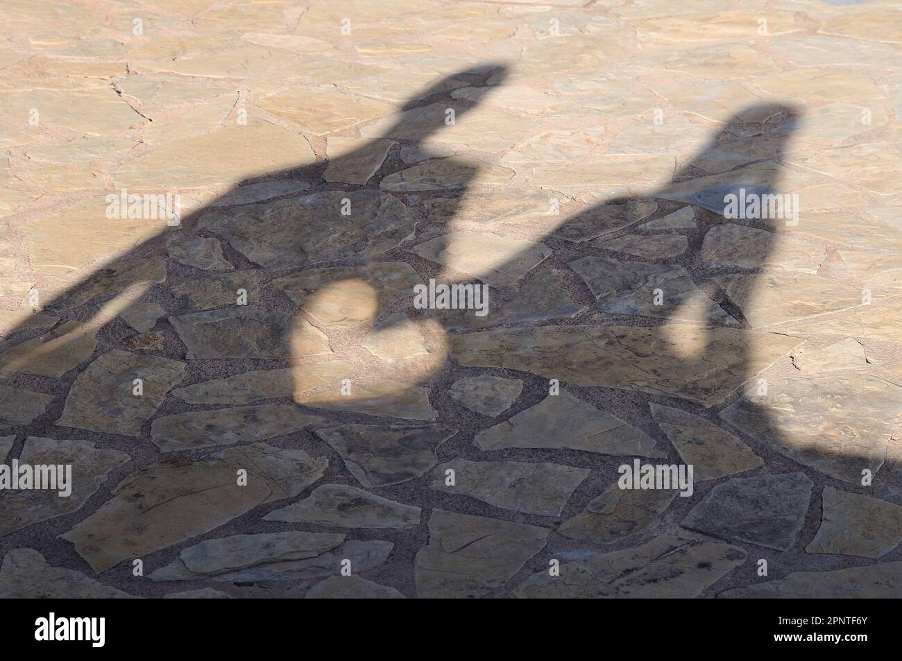 Shadow on stone floor of a couple sitting on a wall holding hands ...