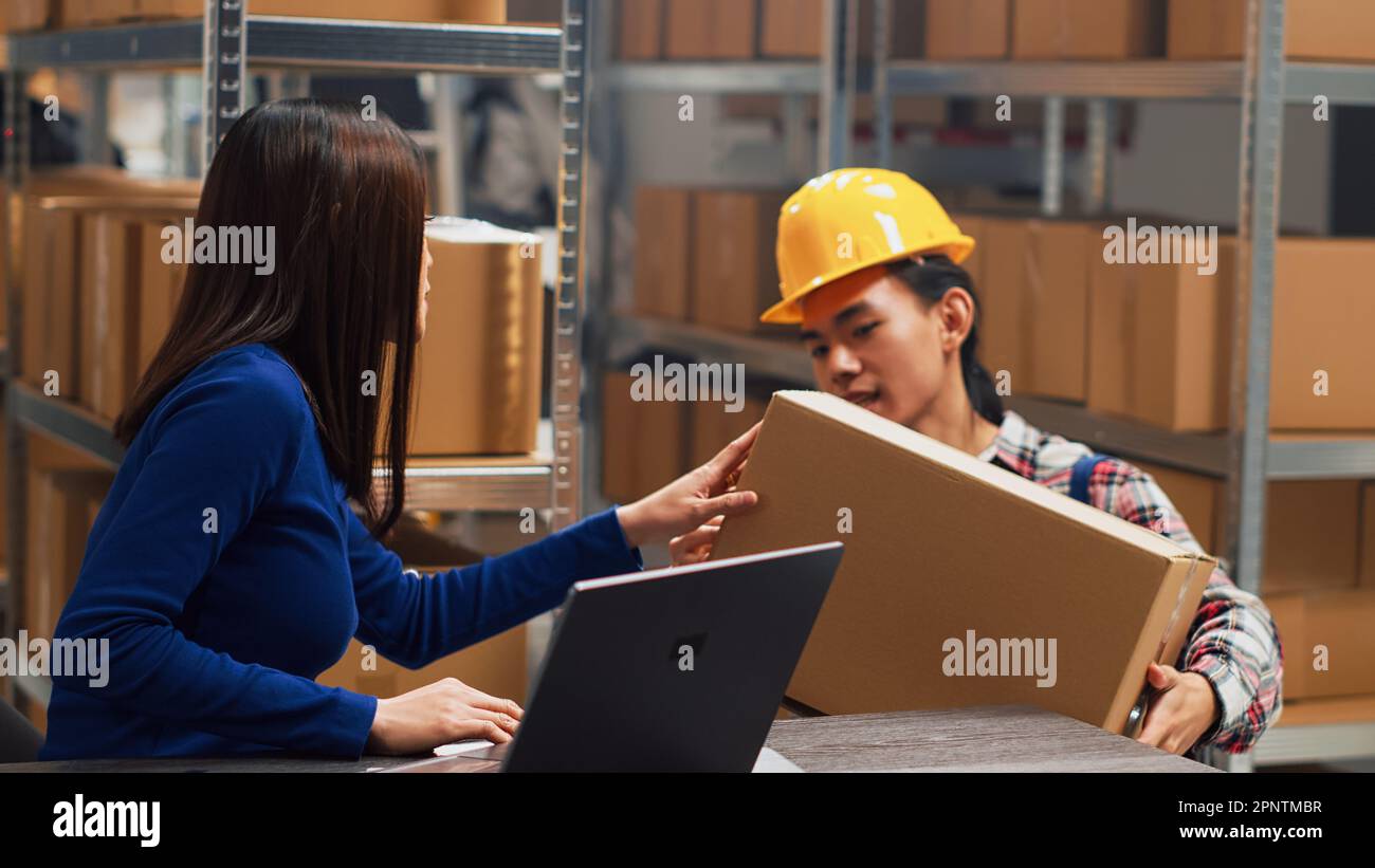 Asian man wheelchair user carrying products boxes in storage room, helping business owner with ...