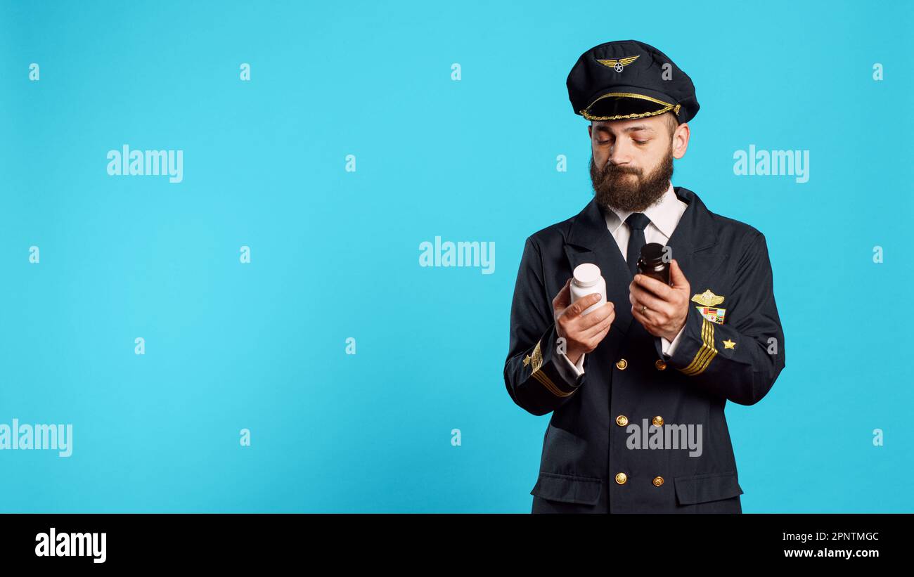 Male aviator looking at bottles of pills in studio, feeling unsure ...