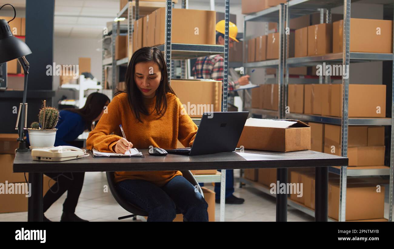Young person doing stock inventory with laptop, writing logistics ...
