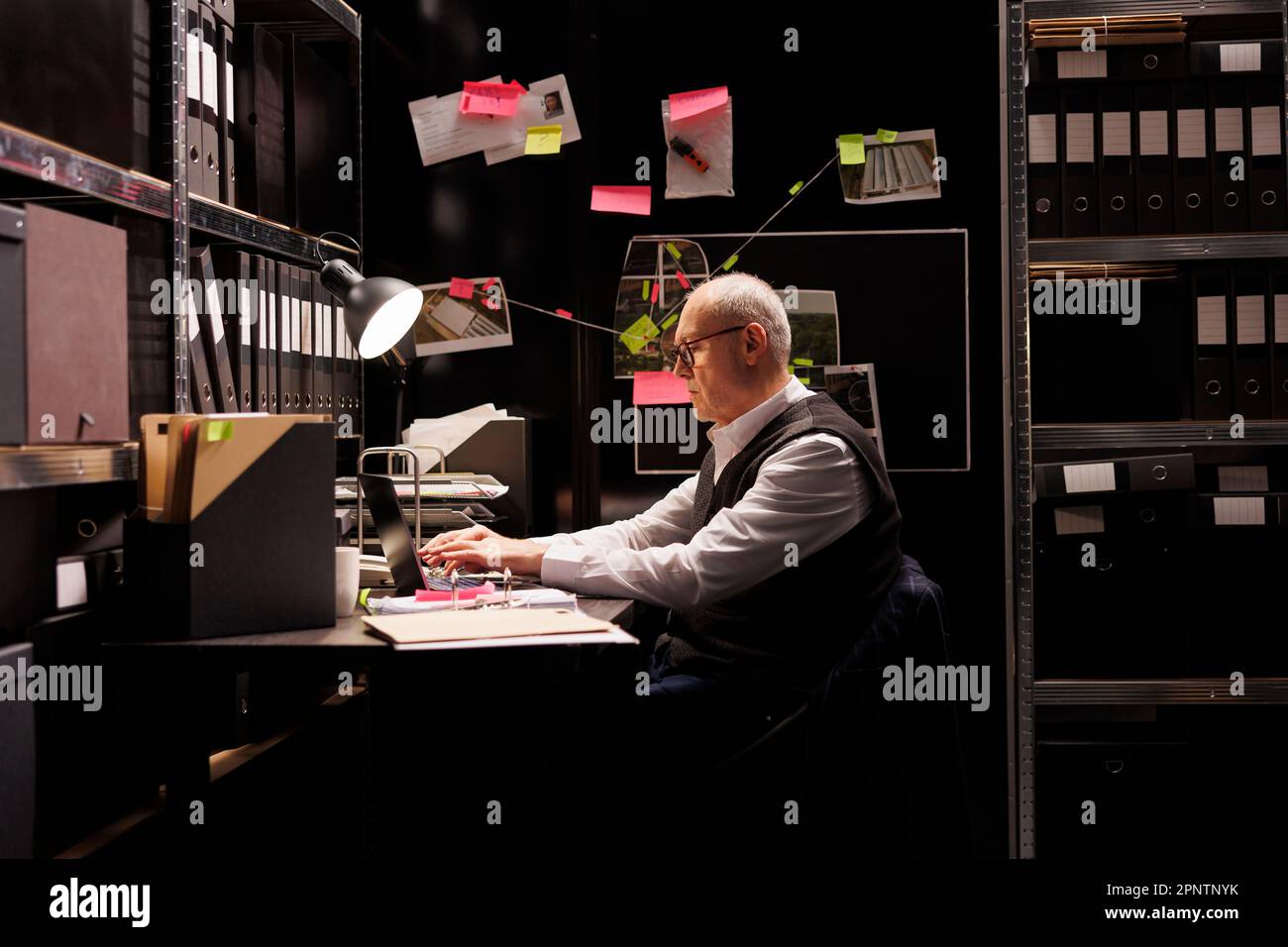 Senior private investigator sitting at desk table in dark room, working ...